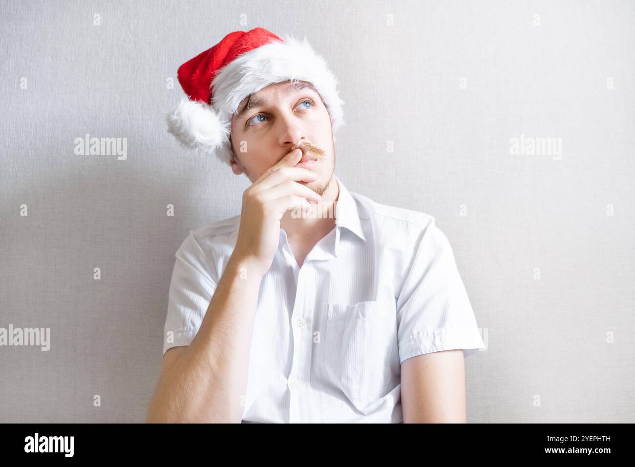 Pensive Man in Santa Hat is Thinking on the White Wall Background in ...