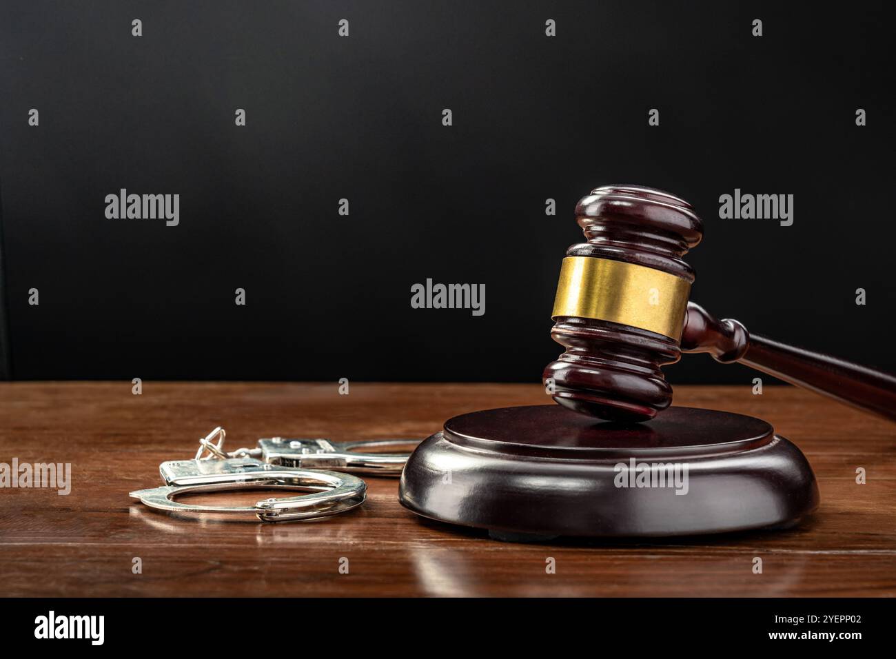 Judge's gavel and a set of handcuffs on a dark colored wooden table ...