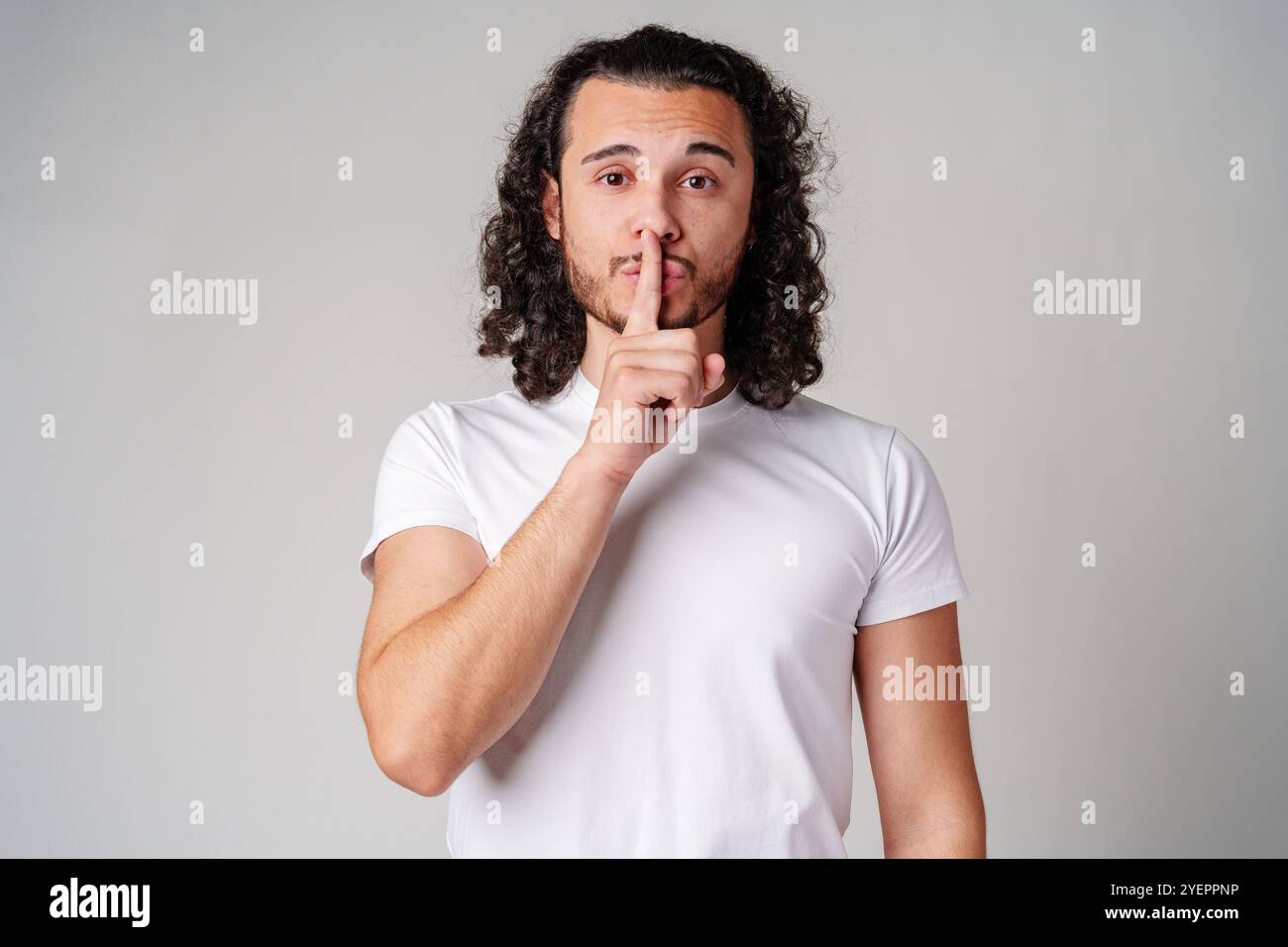 A young man with curly hair demonstrates a hand gesture in a plain ...