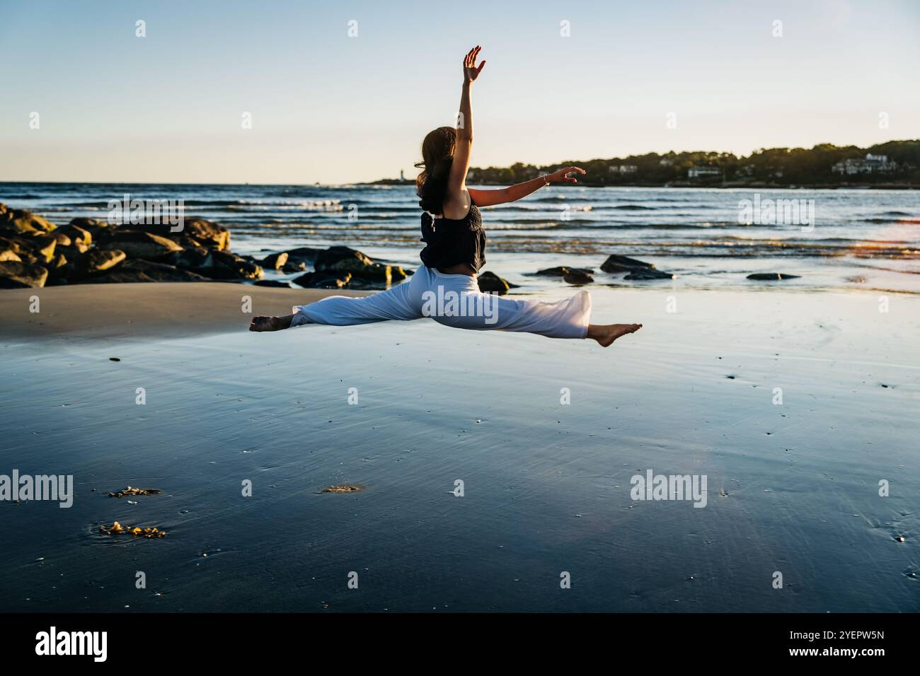 Woman performing a split leap on the beach at sunset, arms extended ...