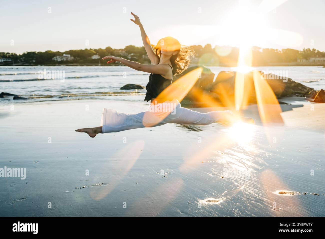 Woman performing a split leap on beach with vibrant sun flares Stock Photo - Alamy