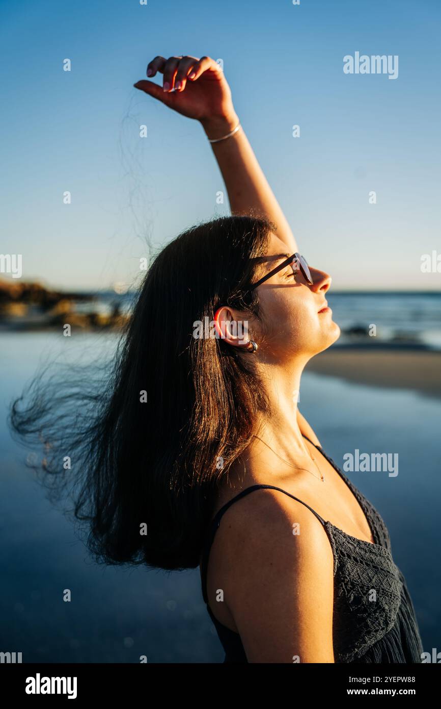Woman basking in sunlight on the beach, arm raised, eyes closed Stock ...
