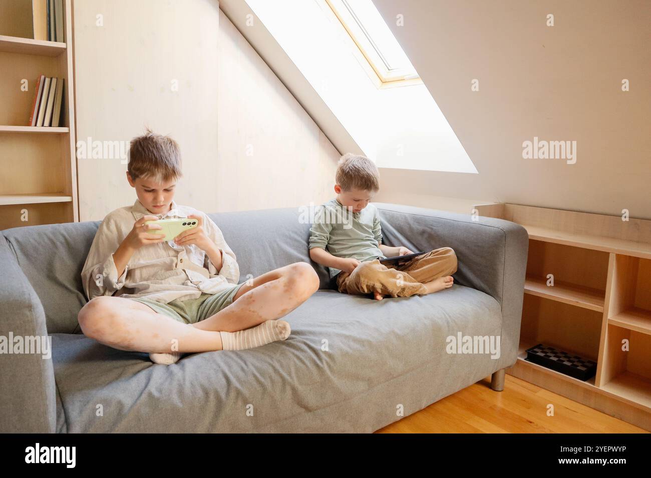 Two brothers bonding over devices in a pastel living room Stock Photo ...