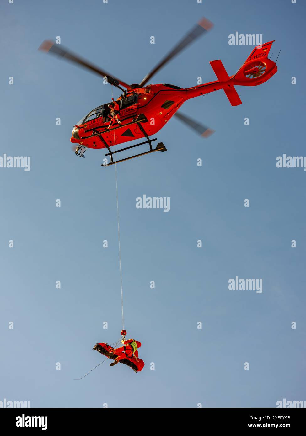 Injured person in a mountain bag with an air rescuer being winched into ...