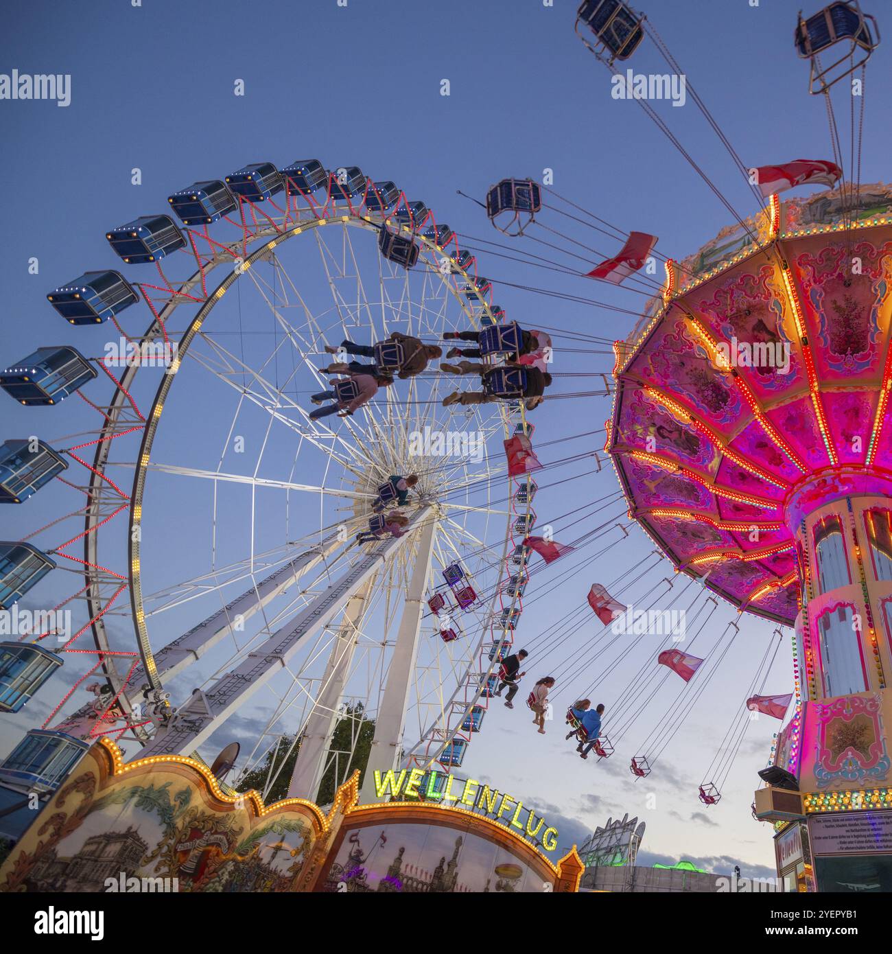 A funfair at dusk with illuminated chain carousel and Ferris wheel ...