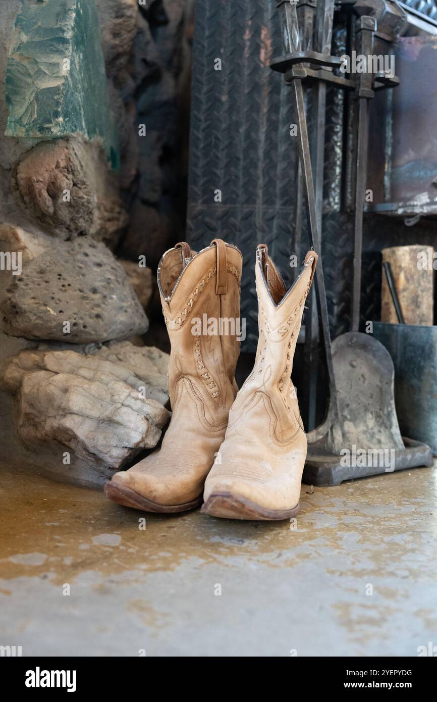 Pair of worn cowboy boots beside a rustic stone and metal backdrop ...