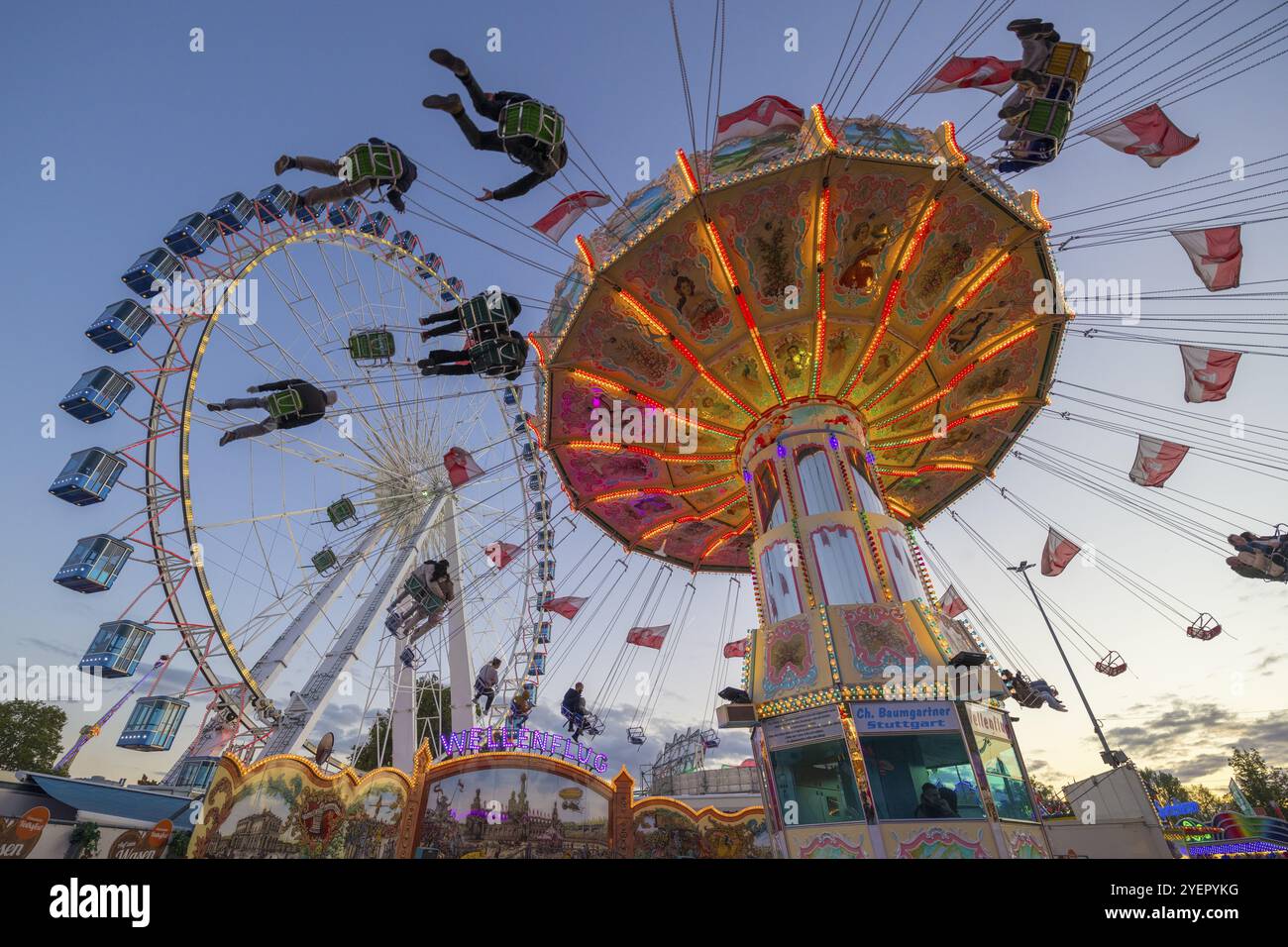 A funfair at dusk with illuminated chain carousel and Ferris wheel ...