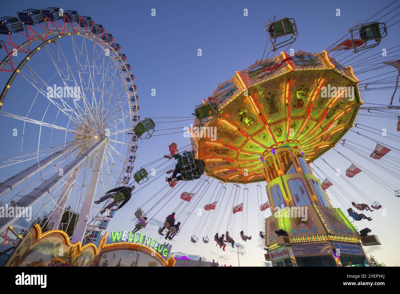 A funfair at dusk with illuminated chain carousel and Ferris wheel ...