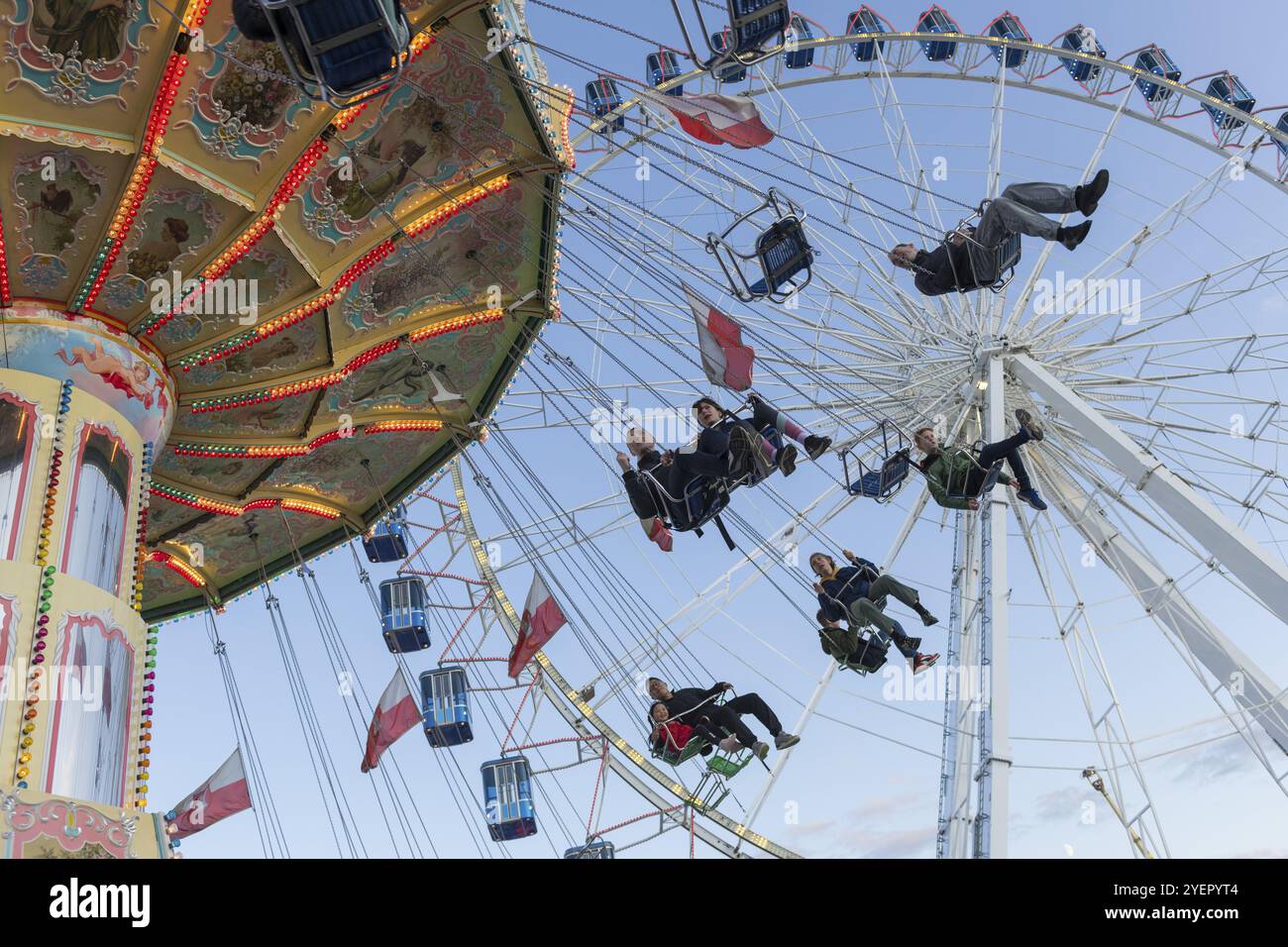 People swinging on a carousel in front of a Ferris wheel in sunny ...