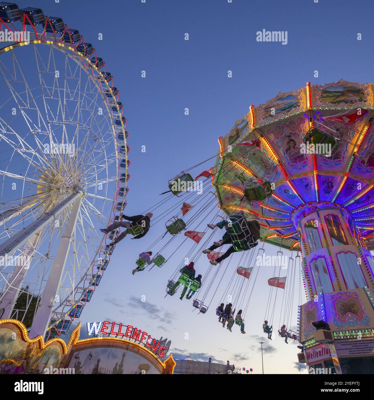 A funfair at dusk with illuminated chain carousel and Ferris wheel ...