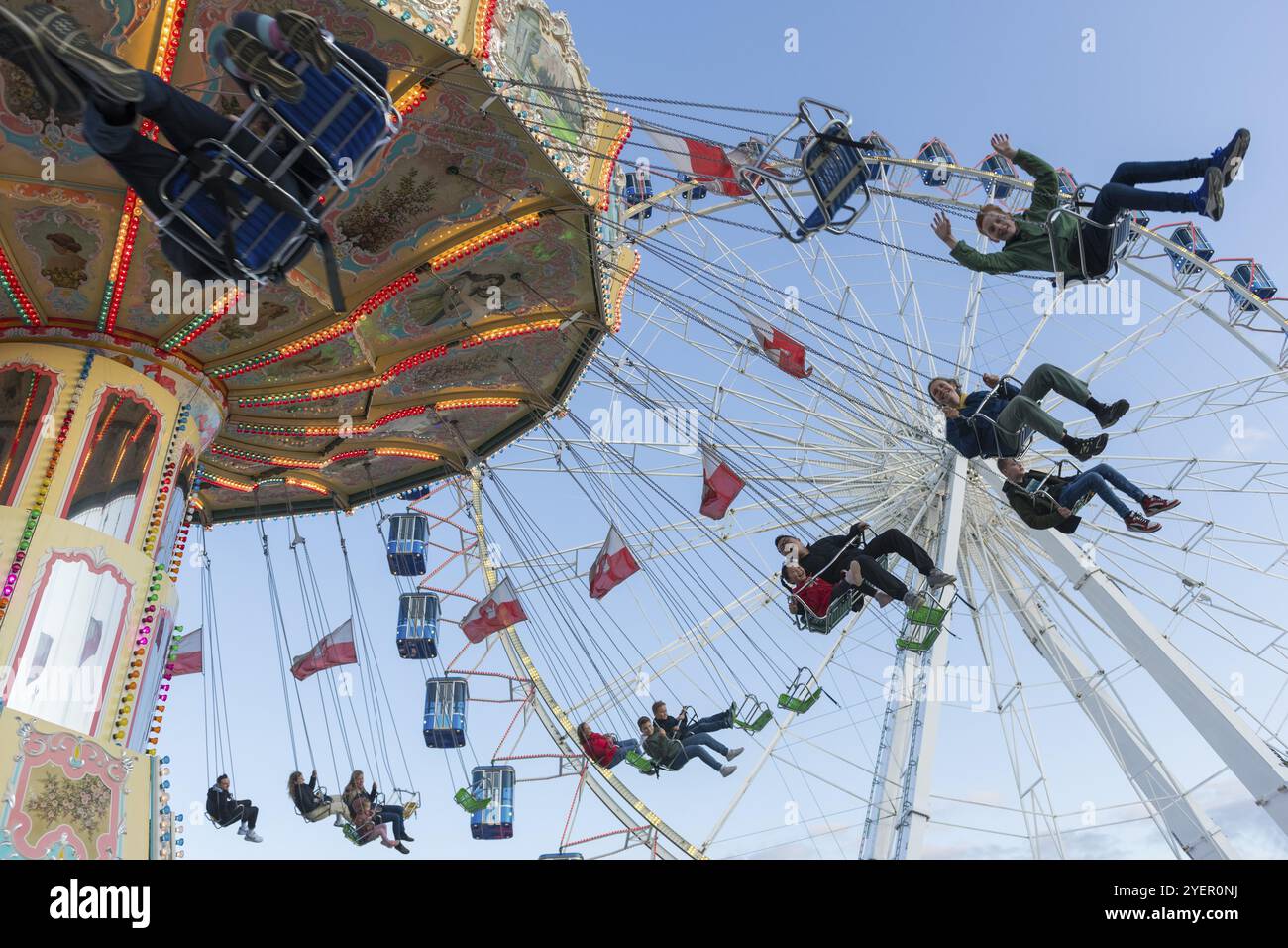 People swinging on a carousel in front of a Ferris wheel in sunny ...