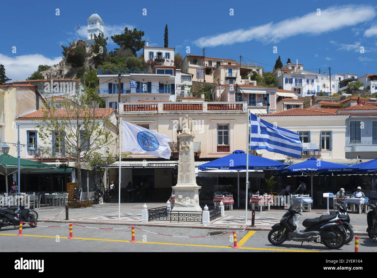 Greek town square with red roofs, a statue and Greek flags, surrounded ...