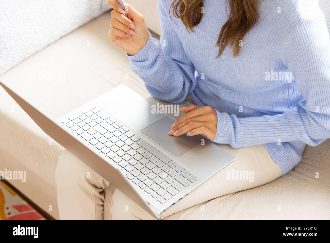 Woman in blue sweater using laptop on couch, working from home. Remote ...