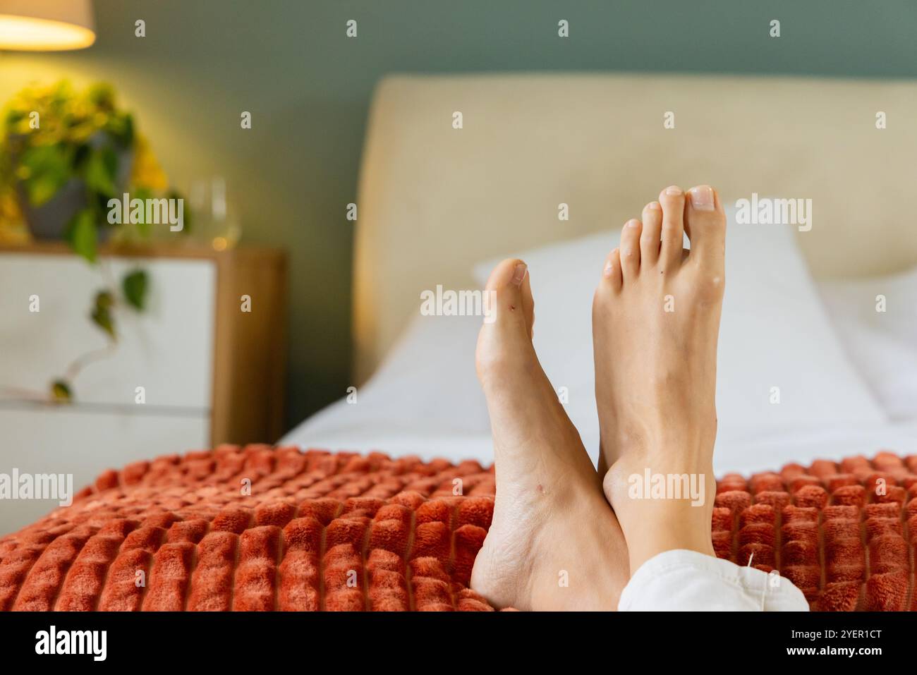 Relaxing at home, woman resting feet on cozy bed with red blanket ...