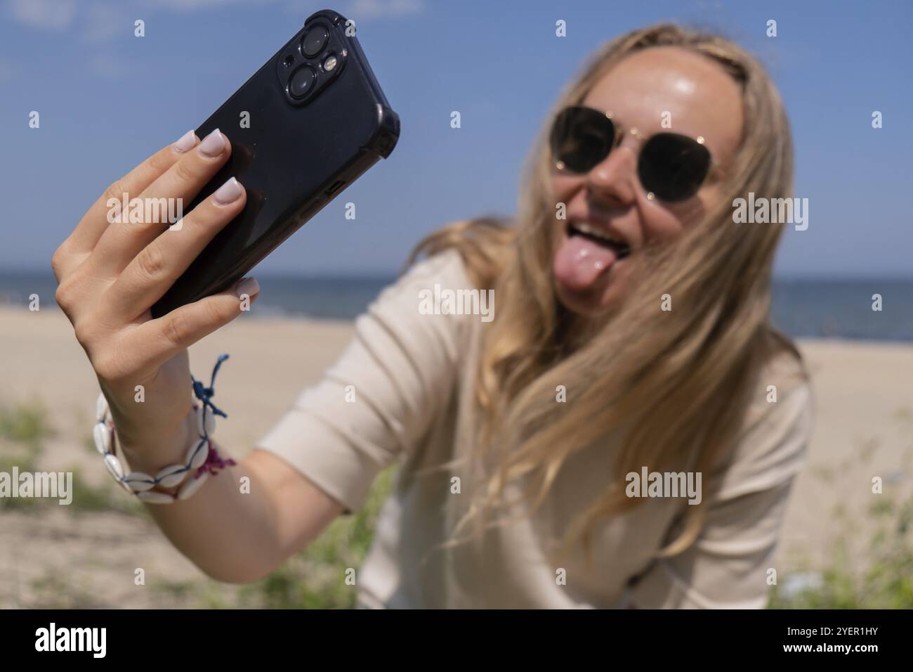 Young woman in sunglasses with shell bracelets holding smartphone ...