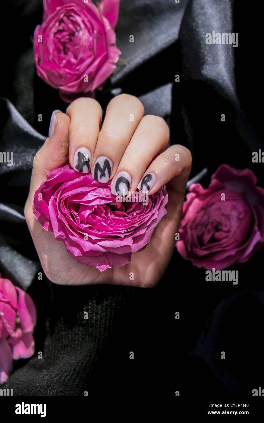 AMOR word on nails manicure hold Pink rose flower on black silk fabric ...