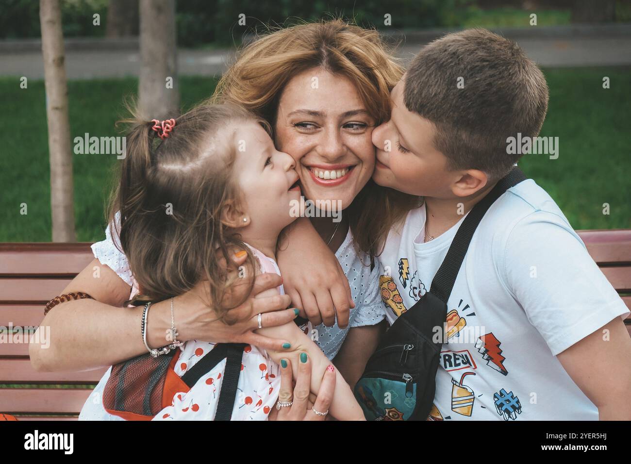 Family portrait. Mother with daughter and son outside in the park. Kids kissing their mom ...