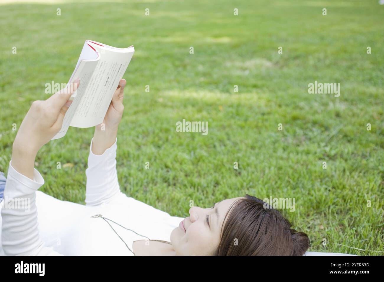 Woman lying on lawn reading book Stock Photo - Alamy