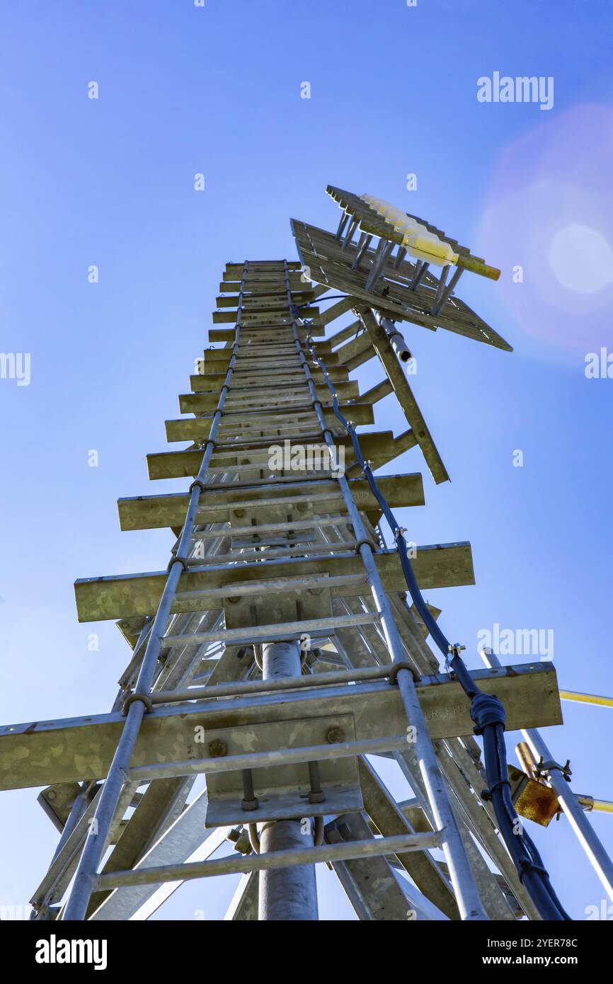 A worms eye view of a tall cellular base station tower against a blue ...