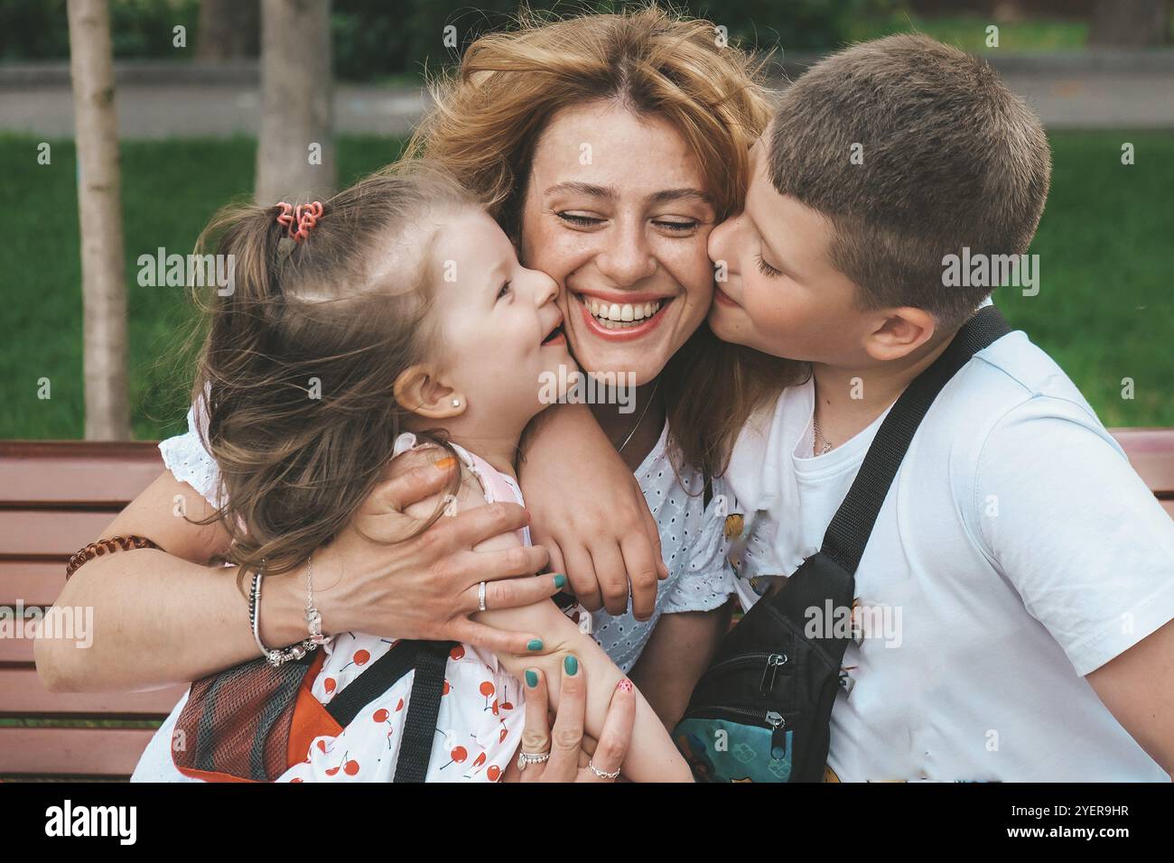 Family portrait. Mother with daughter and son outside in the park. Kids kissing their mom ...
