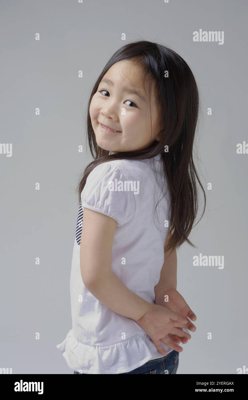 Six-year-old girl looking back with hands behind her back and smiling ...