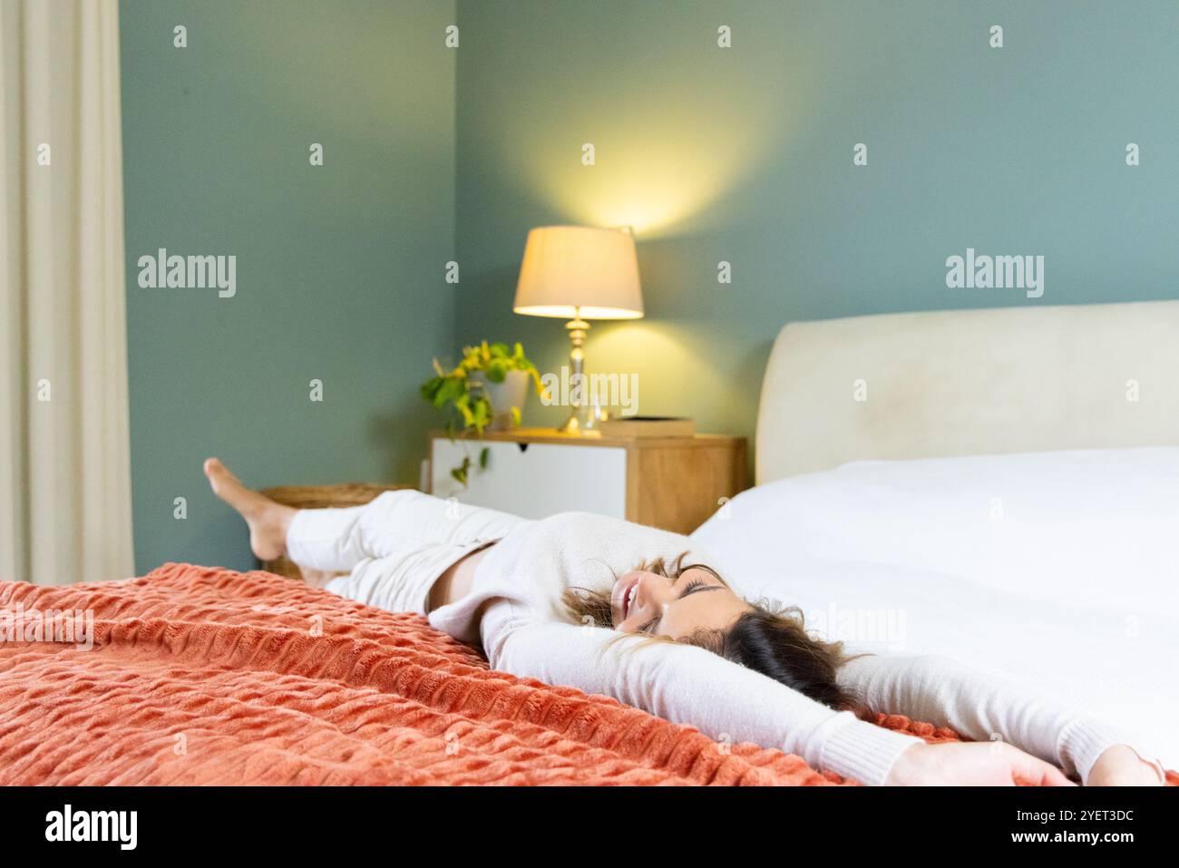 Relaxing on bed, woman stretching joyfully in cozy bedroom with warm ...
