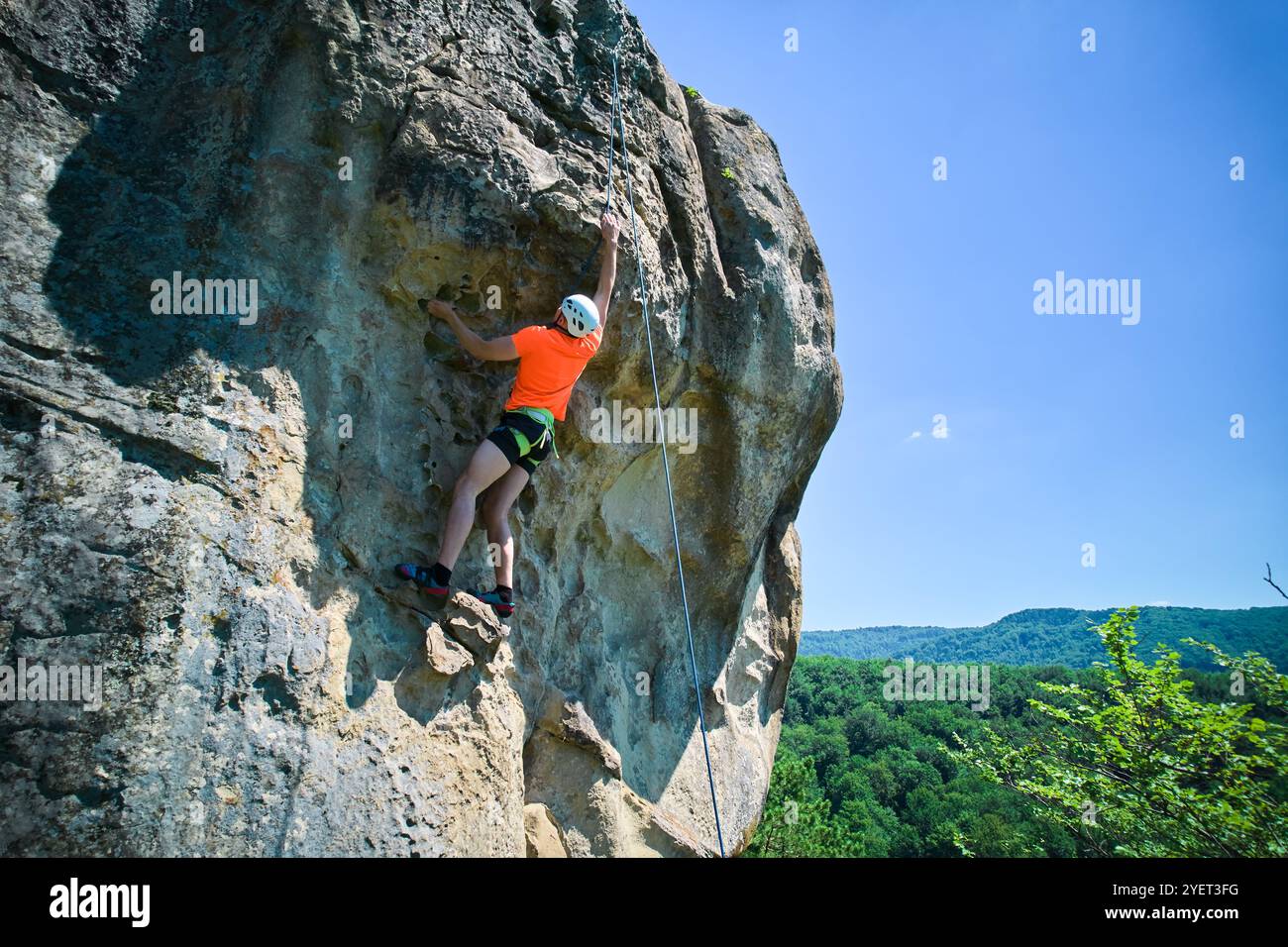 Aerial view of male rock climber ascending rugged limestone cliff with ...