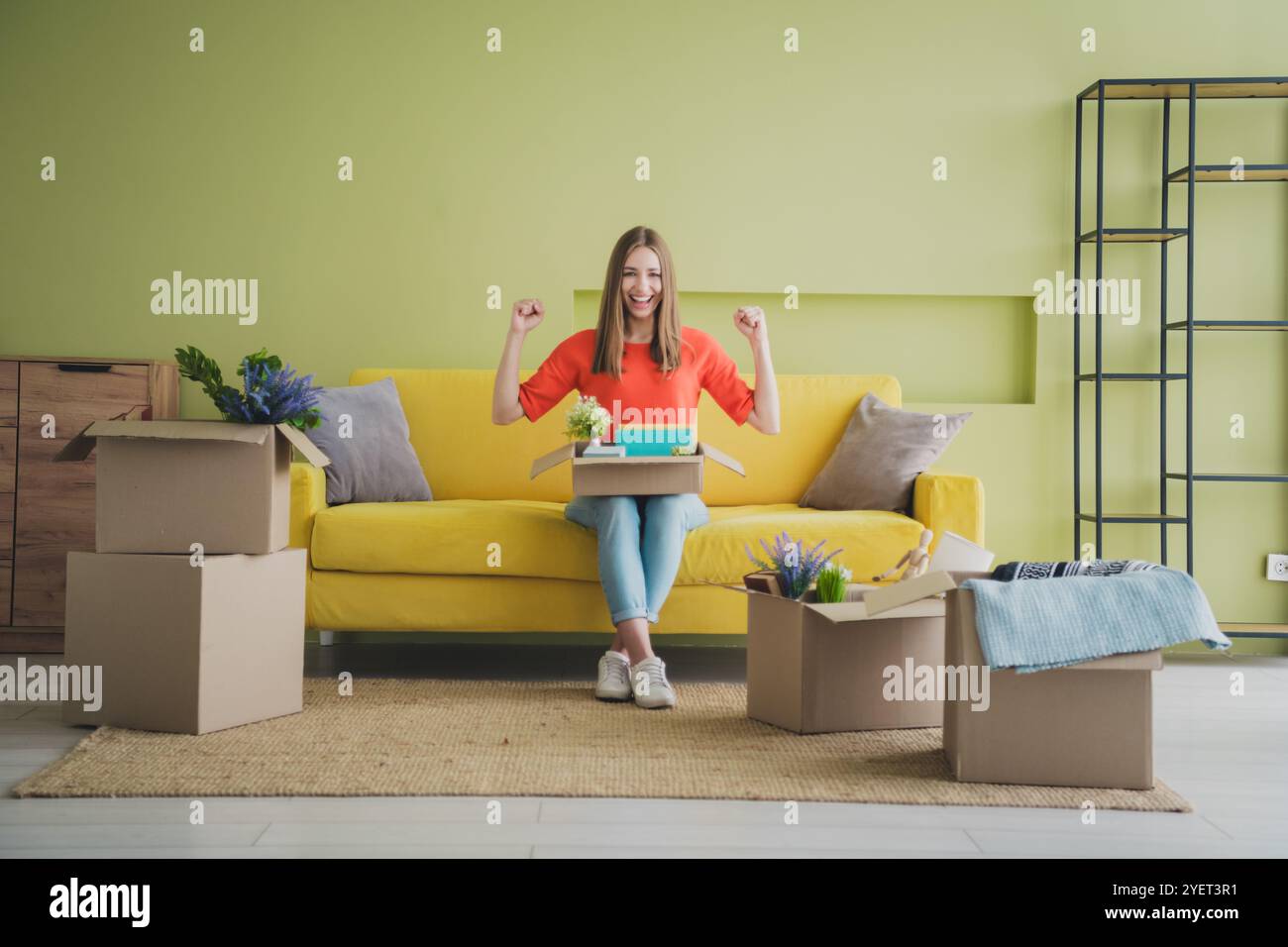 Full body photo of nice young girl sit sofa unpacking winning wear orange clothes enjoy modern ...