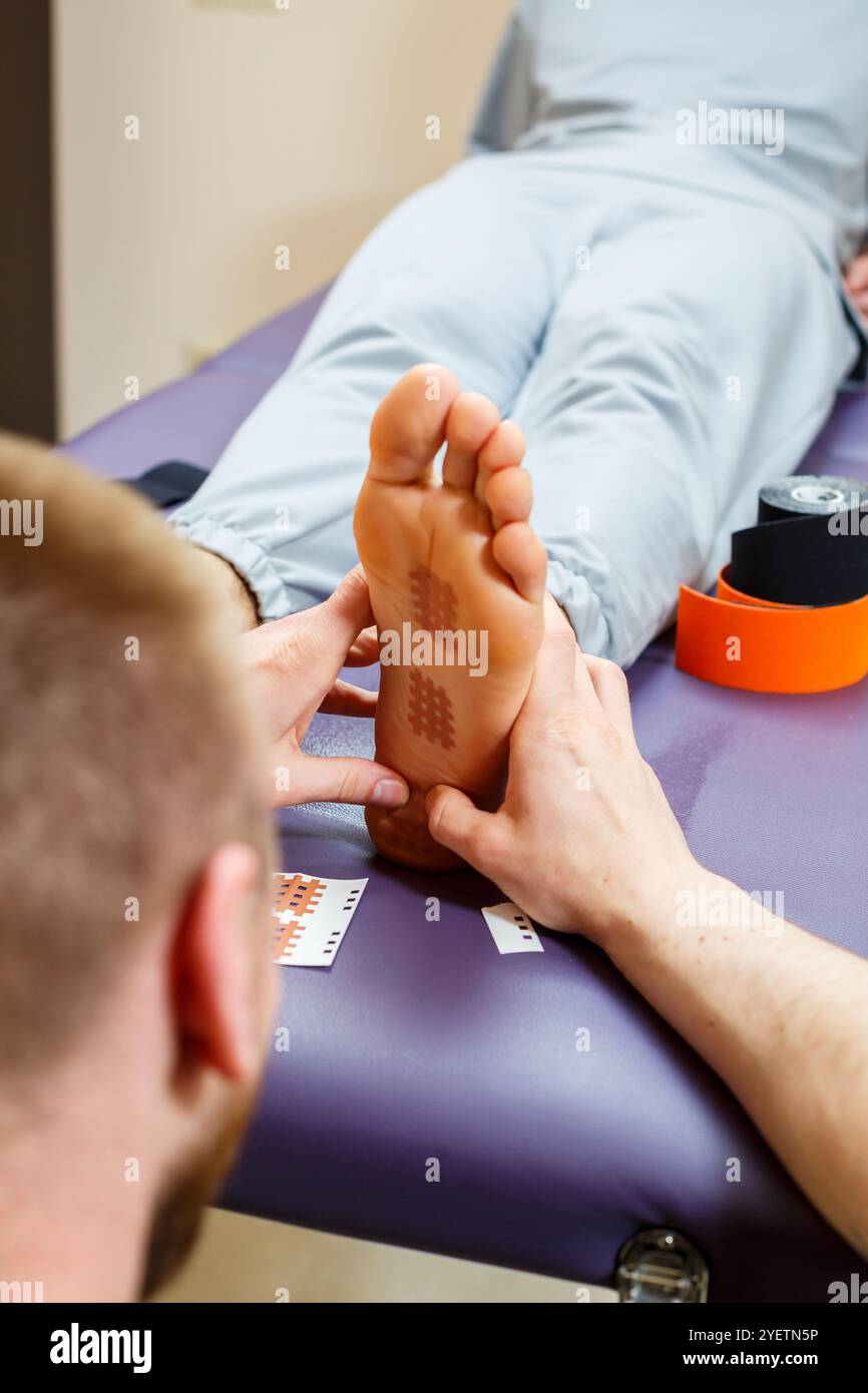 Male physiotherapist doctor massages the feet of a relaxed man sitting ...