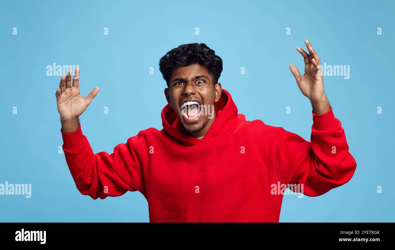 Portrait of emotional Indian man in red hoodie, raising hands upwards ...