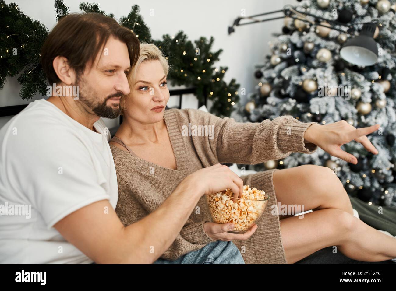 A couple relaxes at home, sharing a bowl of popcorn while watching ...