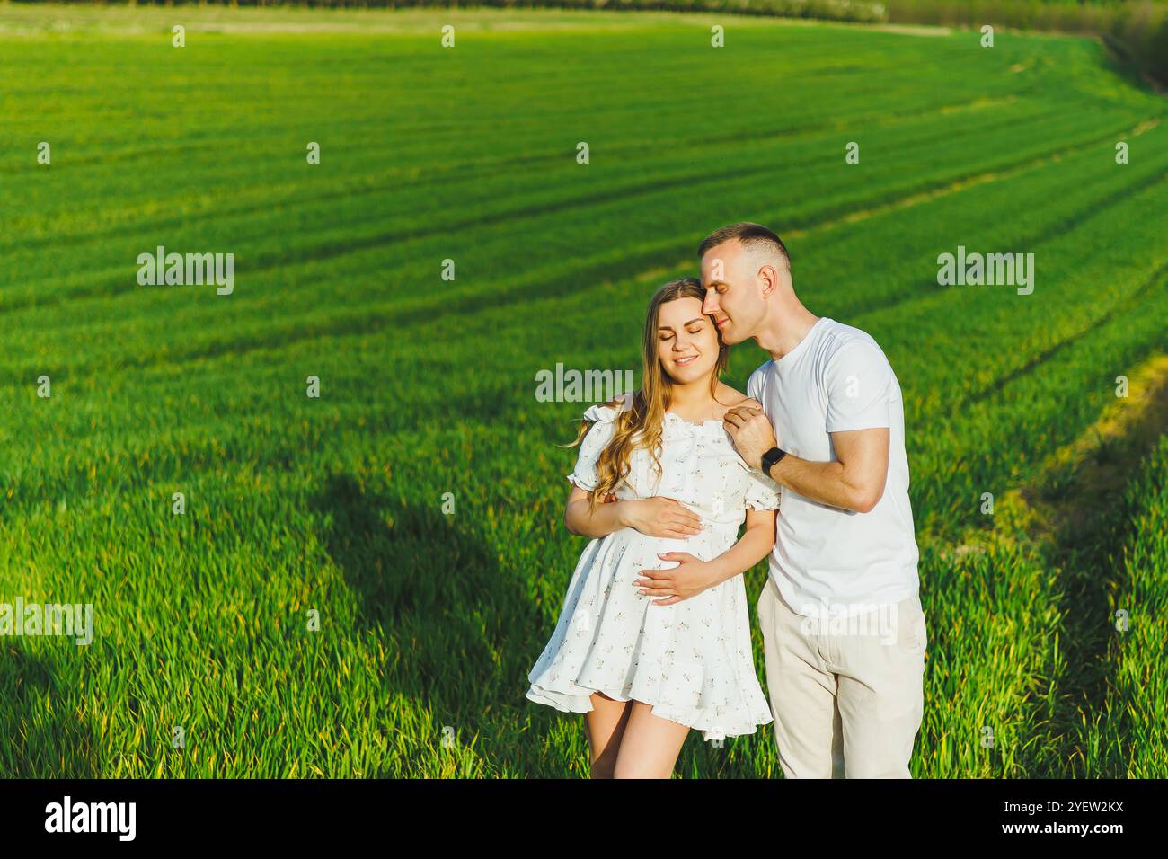 Pregnant couple hugging in a green spring field. Expectant parents in ...