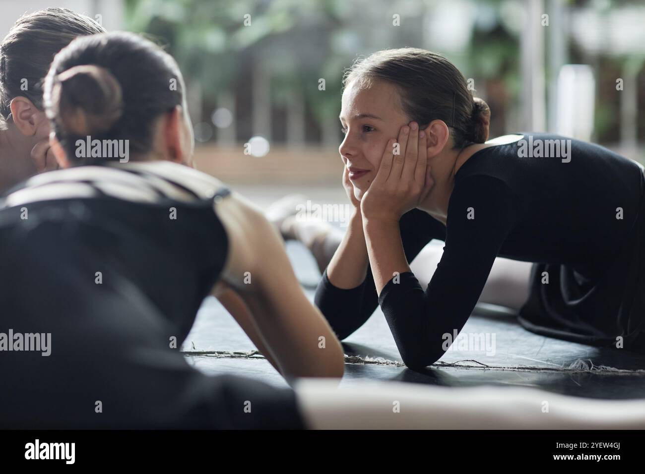Side view of smiling young ballet dancer resting chin on palms while ...
