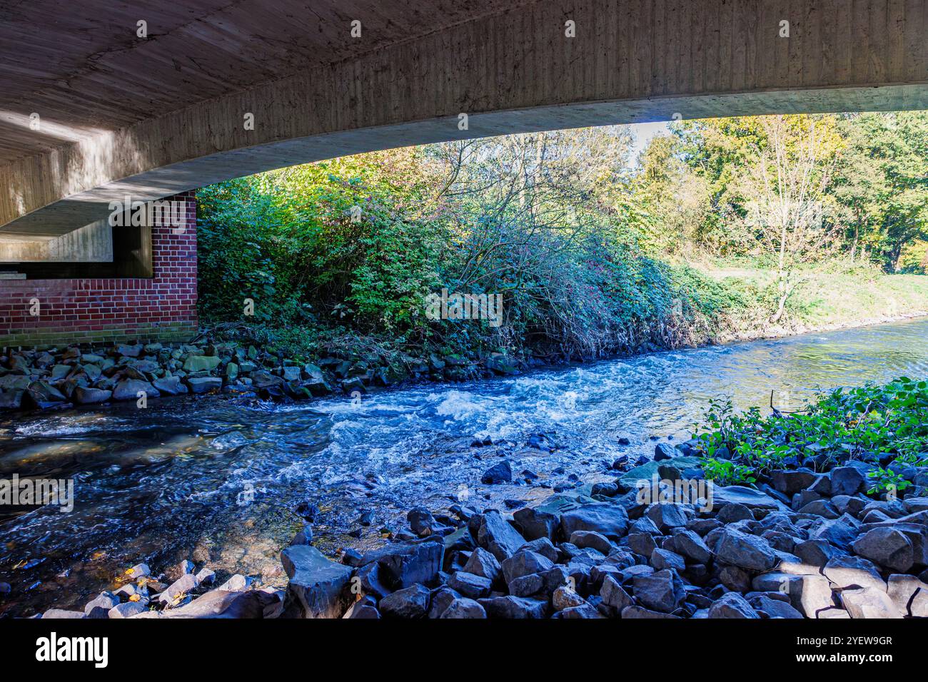 River Wurm with water flowing over stones under vehicle bridge, autumn ...