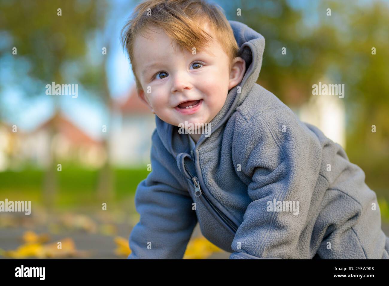 A joyful toddler in a cozy gray jacket leans forward, flashing a bright ...