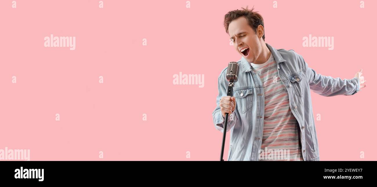 Emotional young man singing in microphone on pink background with space ...