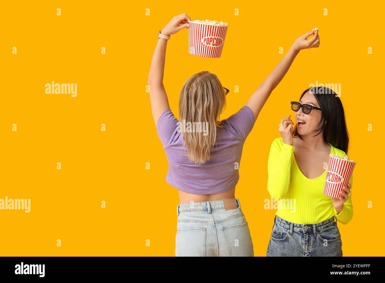 Beautiful young women in 3D glasses with buckets of popcorn on yellow background Stock Photo - Alamy