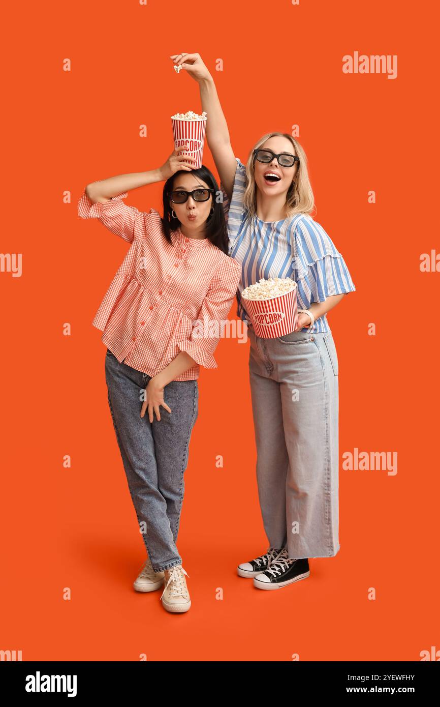 Beautiful young women in 3D glasses with buckets of popcorn on orange background Stock Photo - Alamy