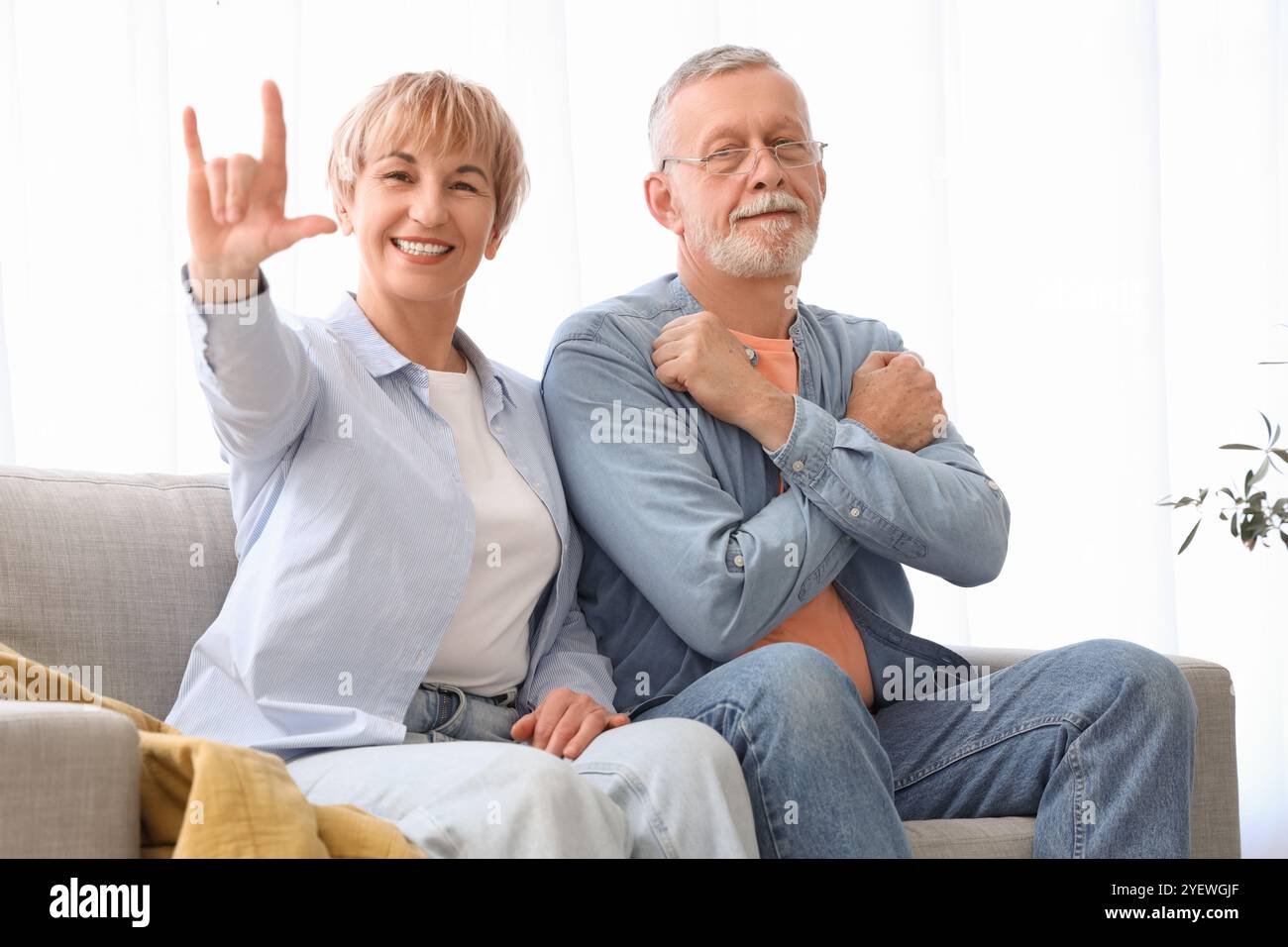 Mature deaf mute couple using sign language on sofa at home Stock Photo ...