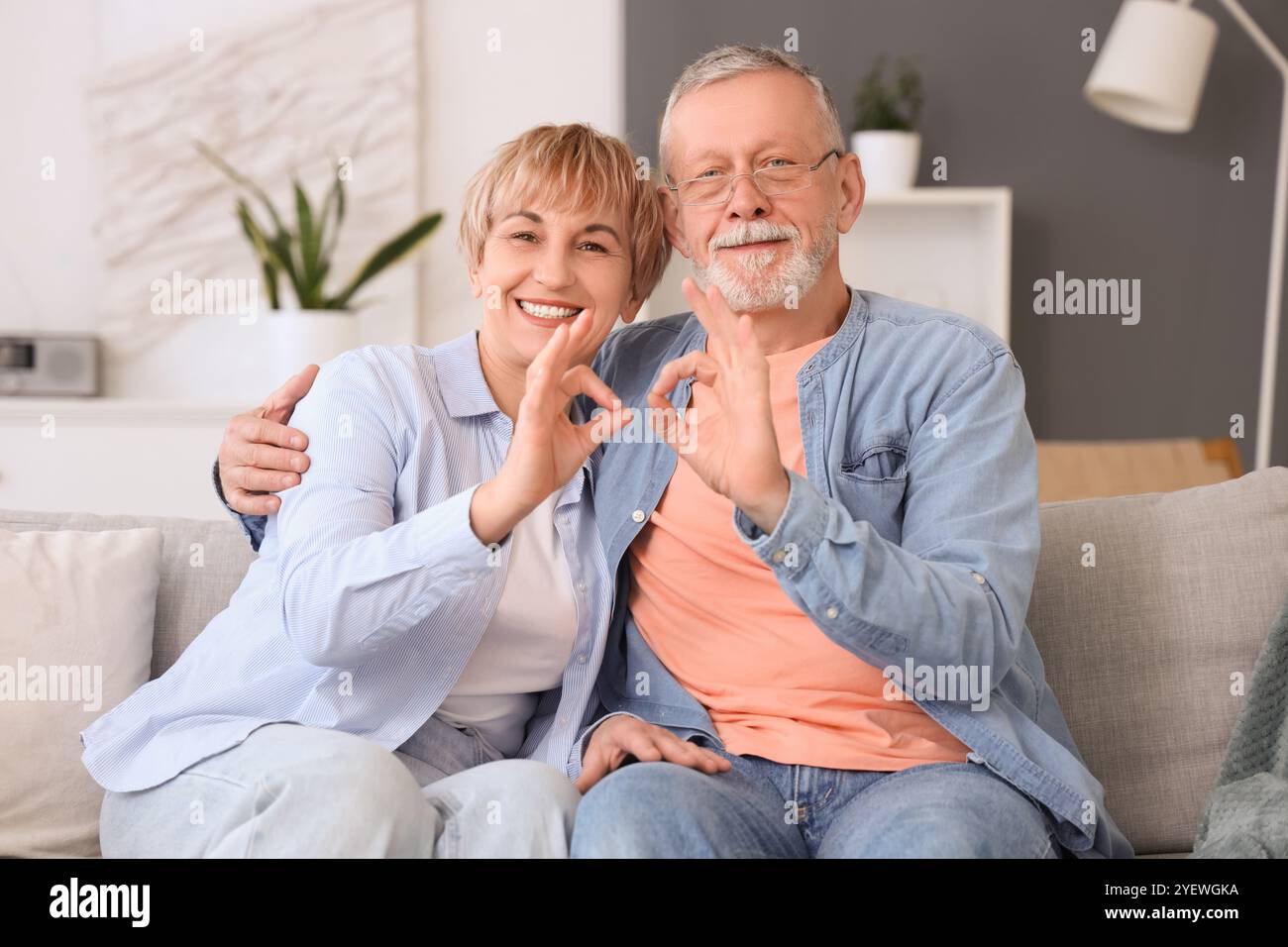 Mature deaf mute couple using sign language on sofa at home Stock Photo ...