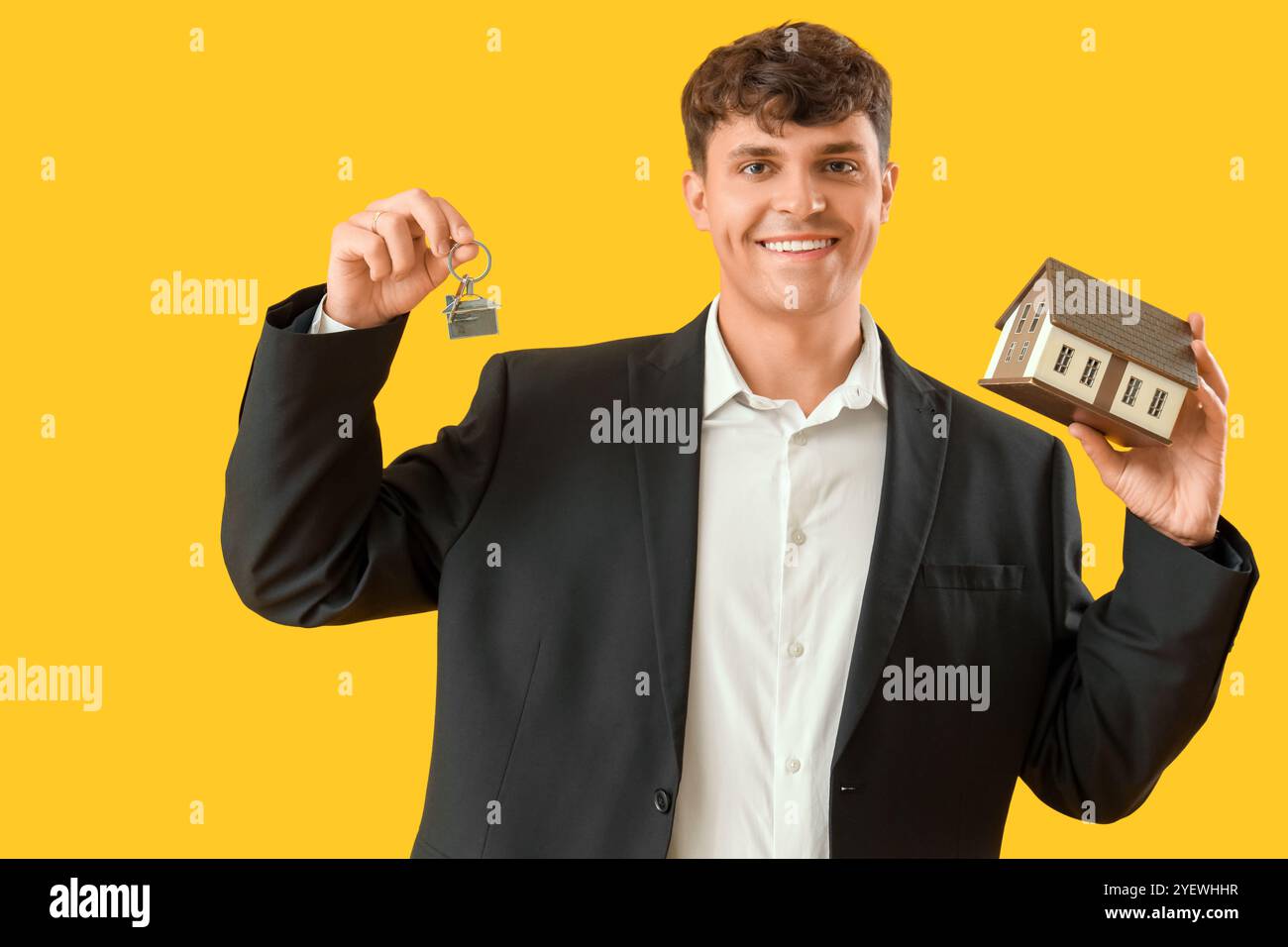 Male real estate agent with house model and key on yellow background ...