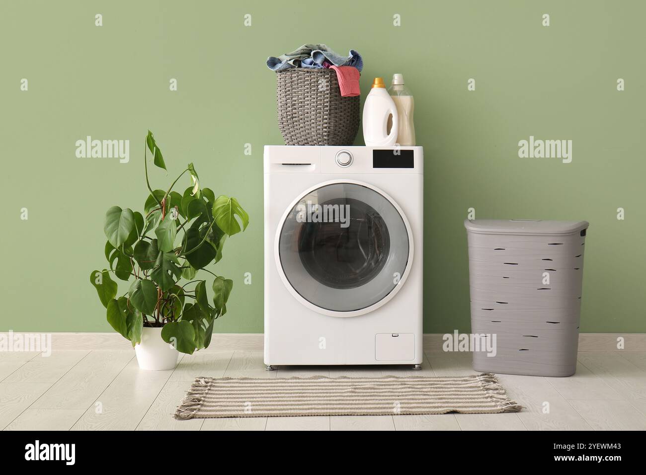 Modern washing machine, basket with laundry and houseplant in room ...