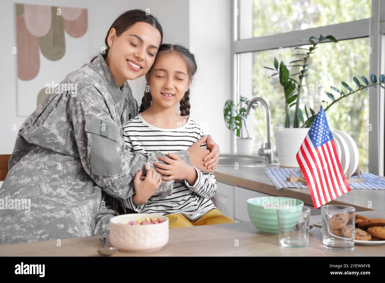 Female soldier with her daughter hugging during breakfast in kitchen ...