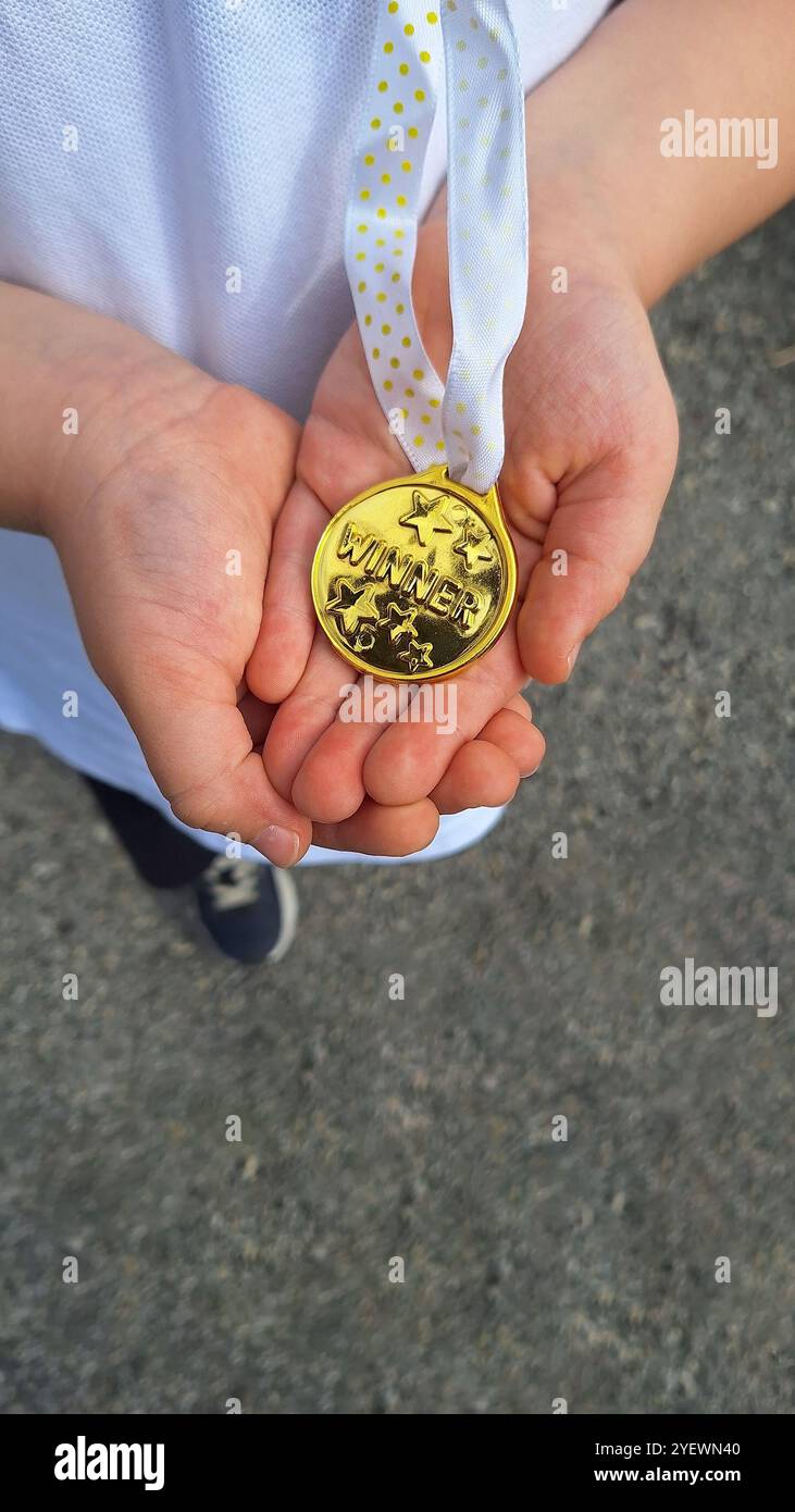 Child proudly holding a first place gold medal with the word WINNER on ...