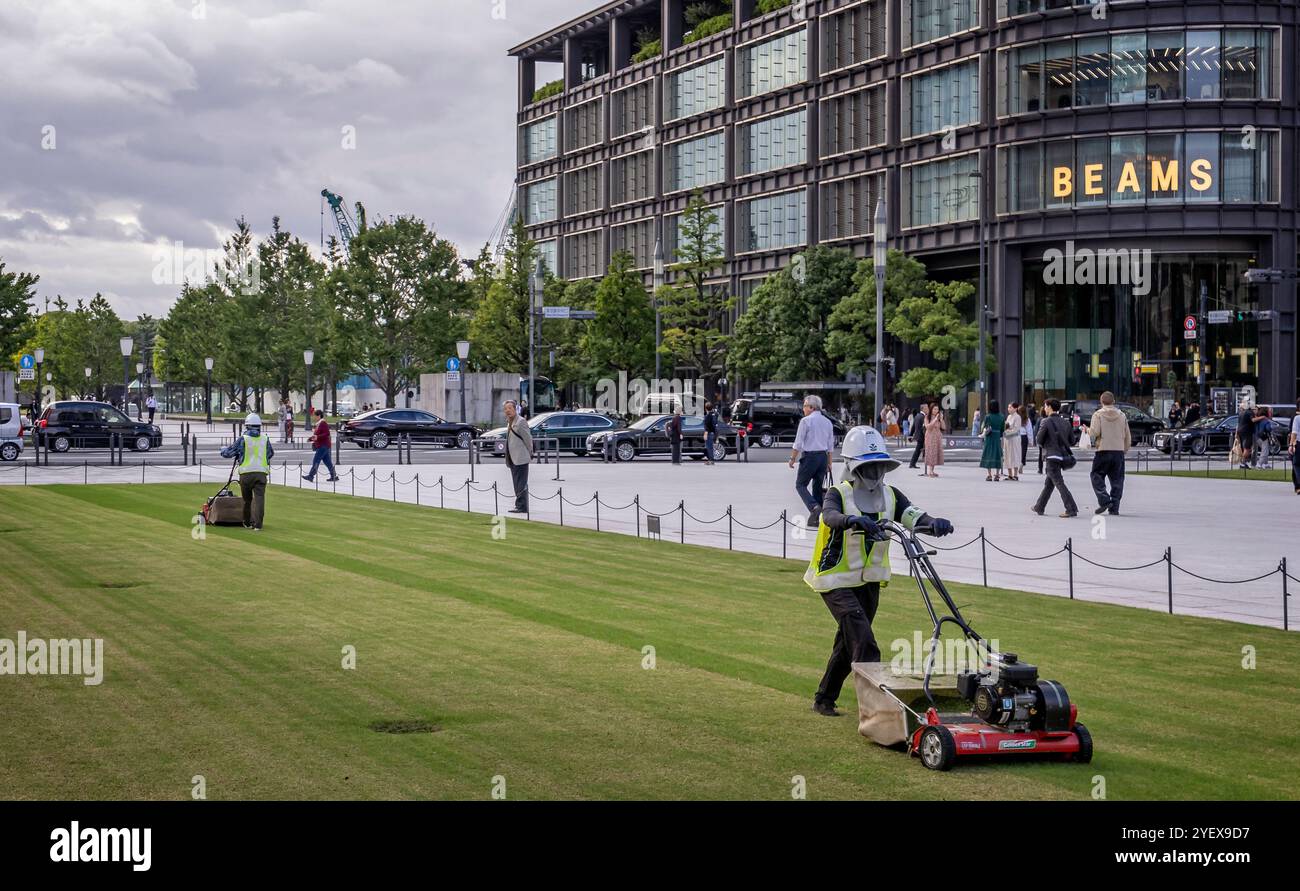 Japanese workers in uniform mowing the lawns in front of Tokyo Station ...