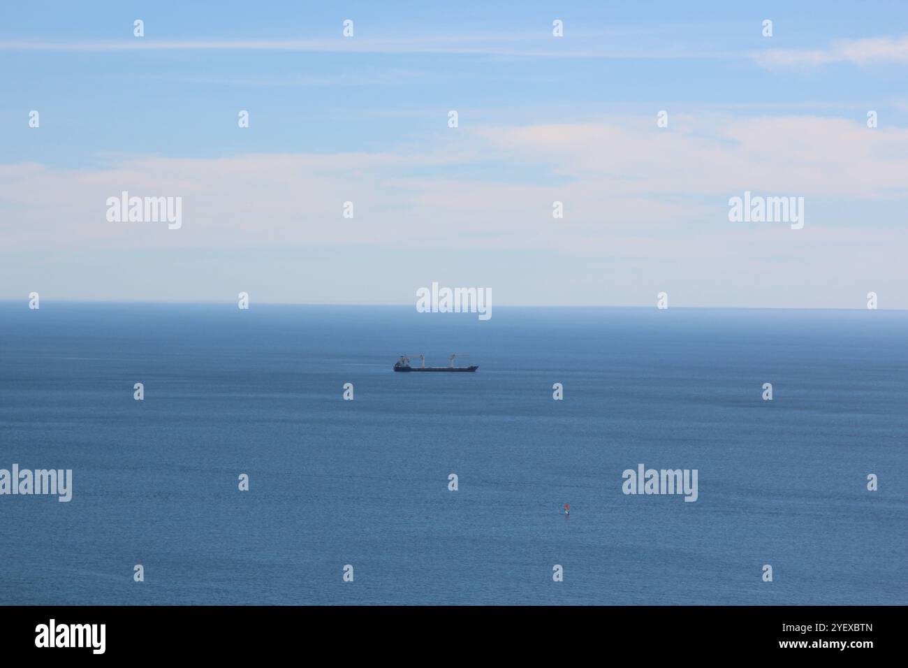 A solitary cargo ship navigates the calm, open sea under a clear blue ...