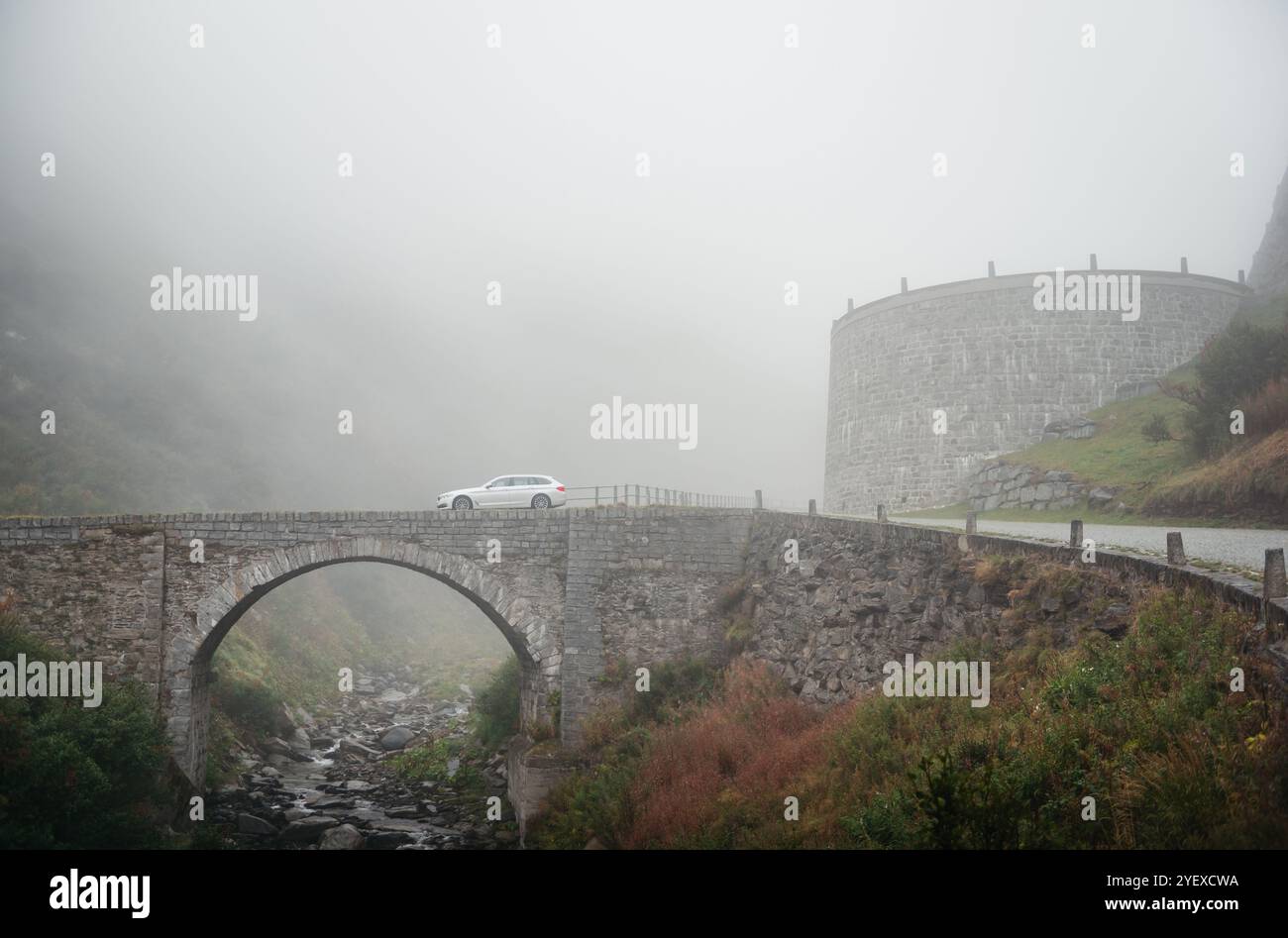 White BMW car on a stone bridge over the mountain river on foggy day ...