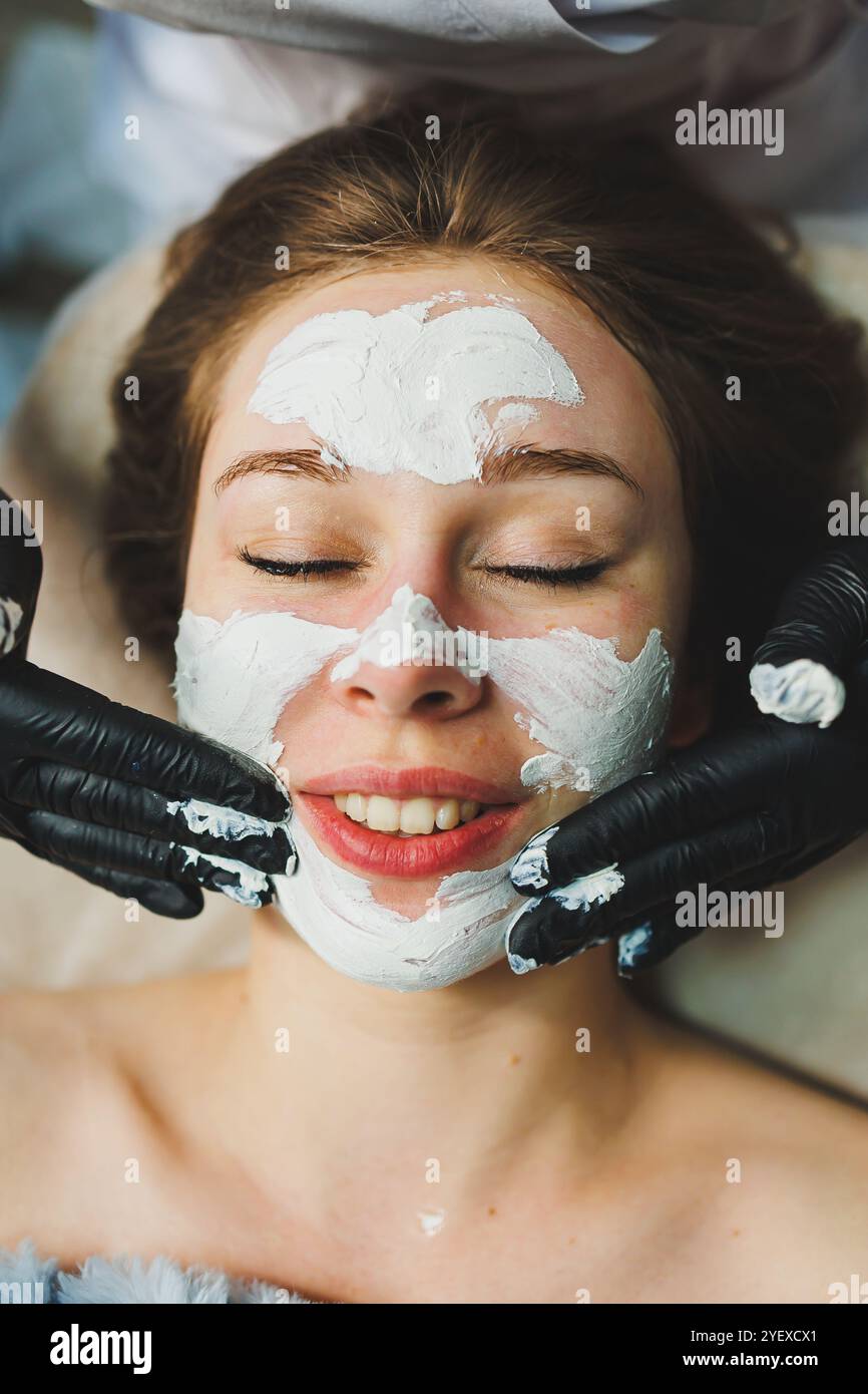 The hands of a beautician apply a mask to a woman's face in a spa salon ...