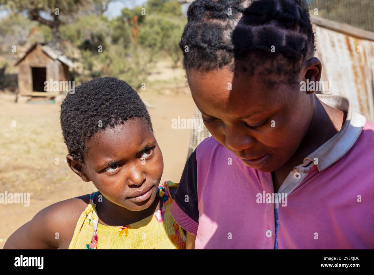 village african child girl, looking at her mother, standing in the yard ...
