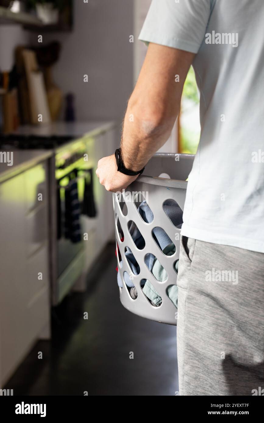 senior man carrying laundry basket in kitchen, focusing on household ...
